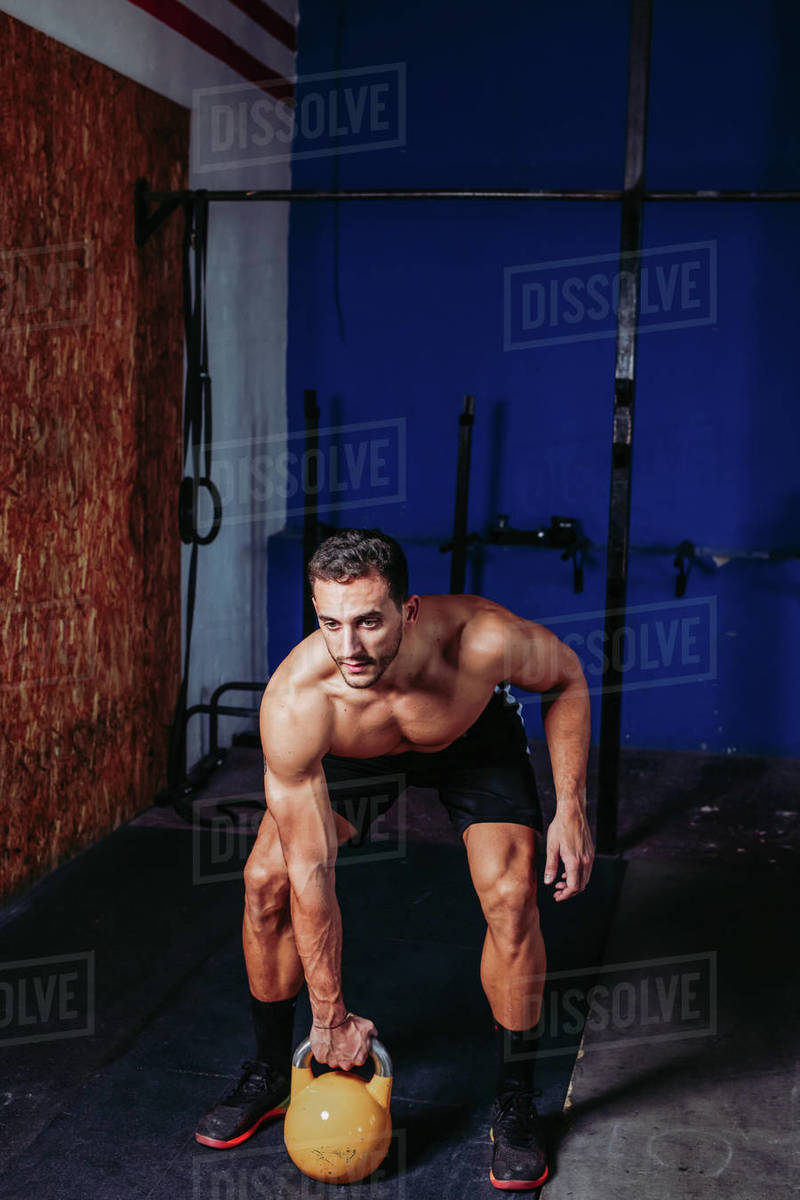 Determined male athlete working hard in gym while doing kettlebell ...