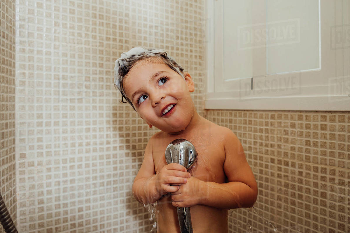 Smiling little child with foam on head standing in bathroom with shower ...
