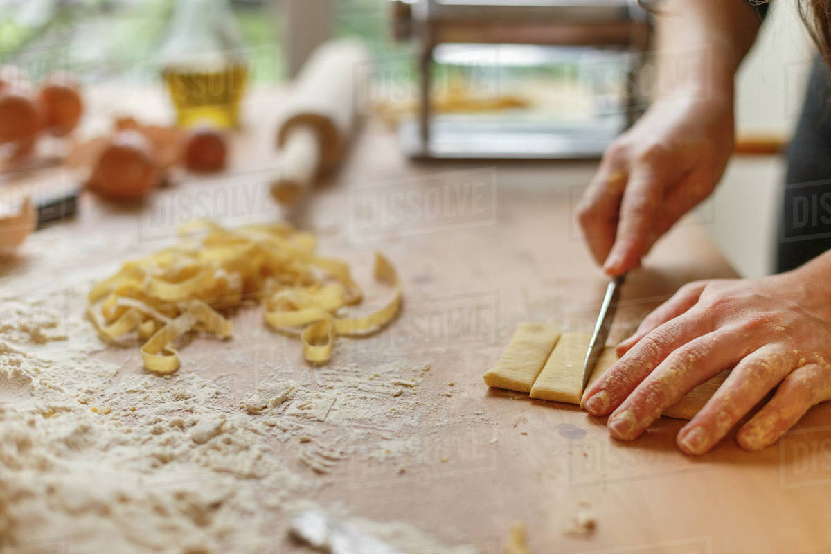 Faceless cook cutting dough into thin strips by knife on wooden table ...