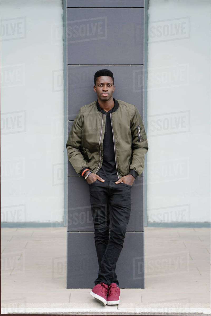 Full body confident African American male with hands in pockets leaning ...