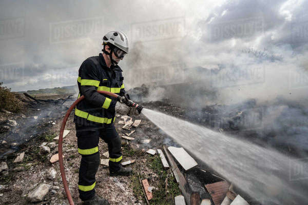 Side view of brave fireman in protective uniform standing with hose and ...