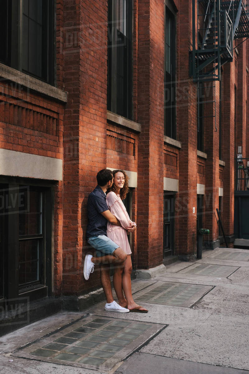 Loving couple cuddling and kissing while standing near brick building ...