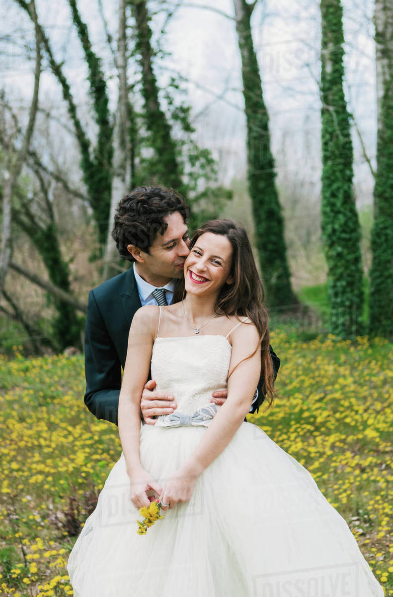 Happy groom in elegant suit hugging smiling bride with yellow ...
