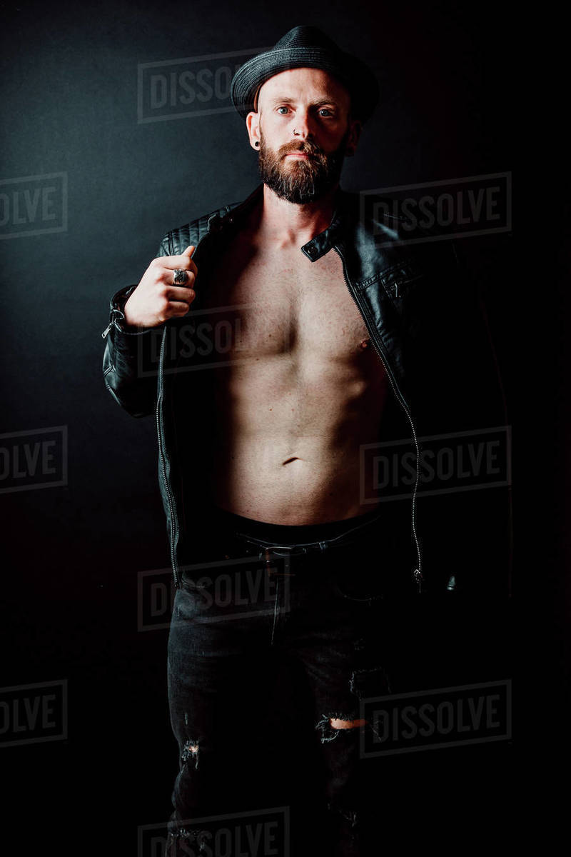 Shirtless cool hipster in hat adjusting leather jacket and looking at ...