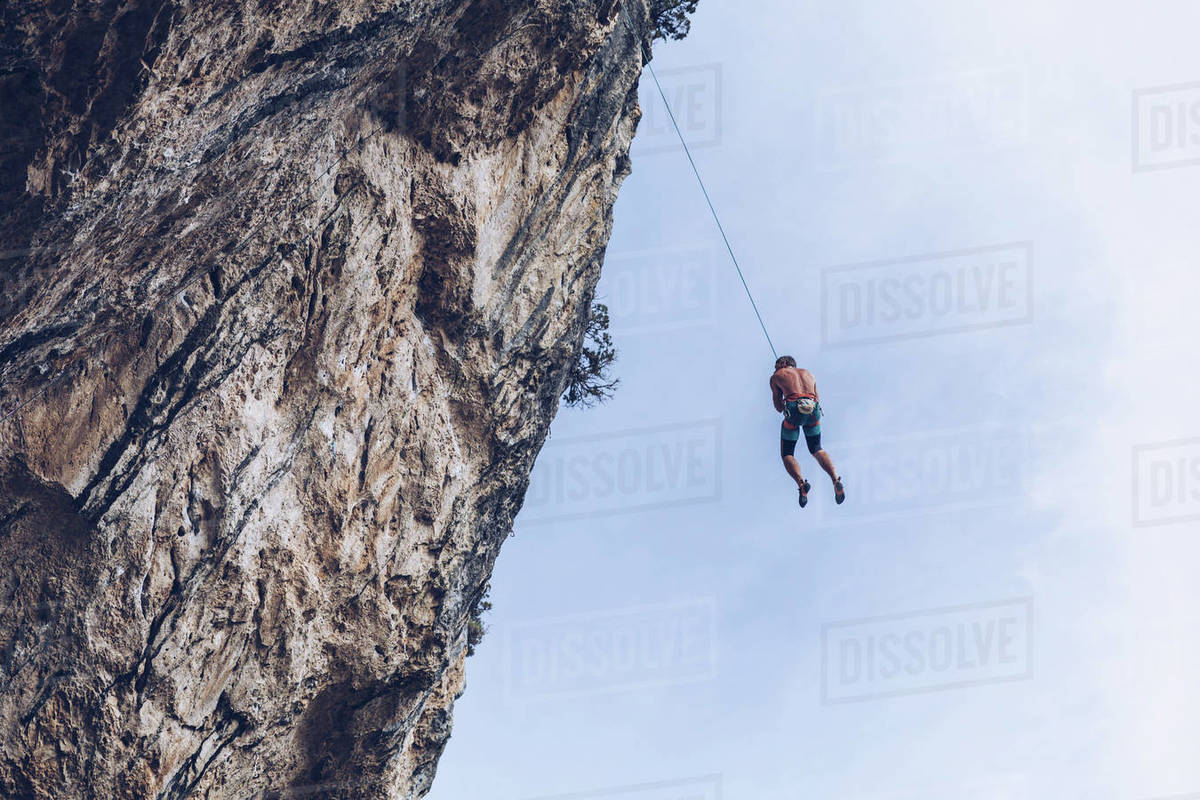 From below unrecognizable climber hanging on rope on rough cliff ...