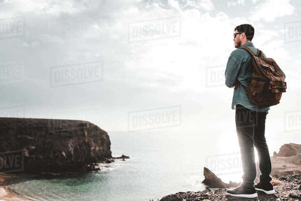 Back view of young tourist on high mountain near sea and cloudy sky ...