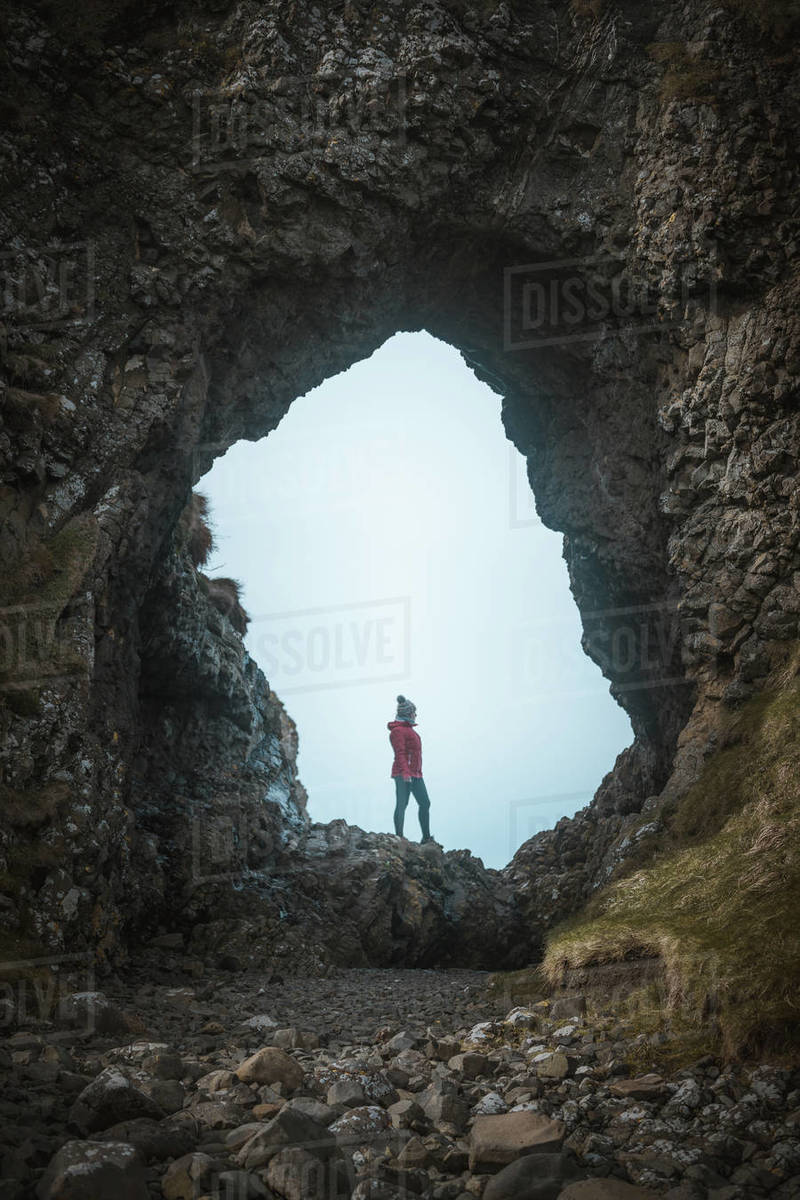 Side view of female in warm outfit standing on cliff edge within cave ...