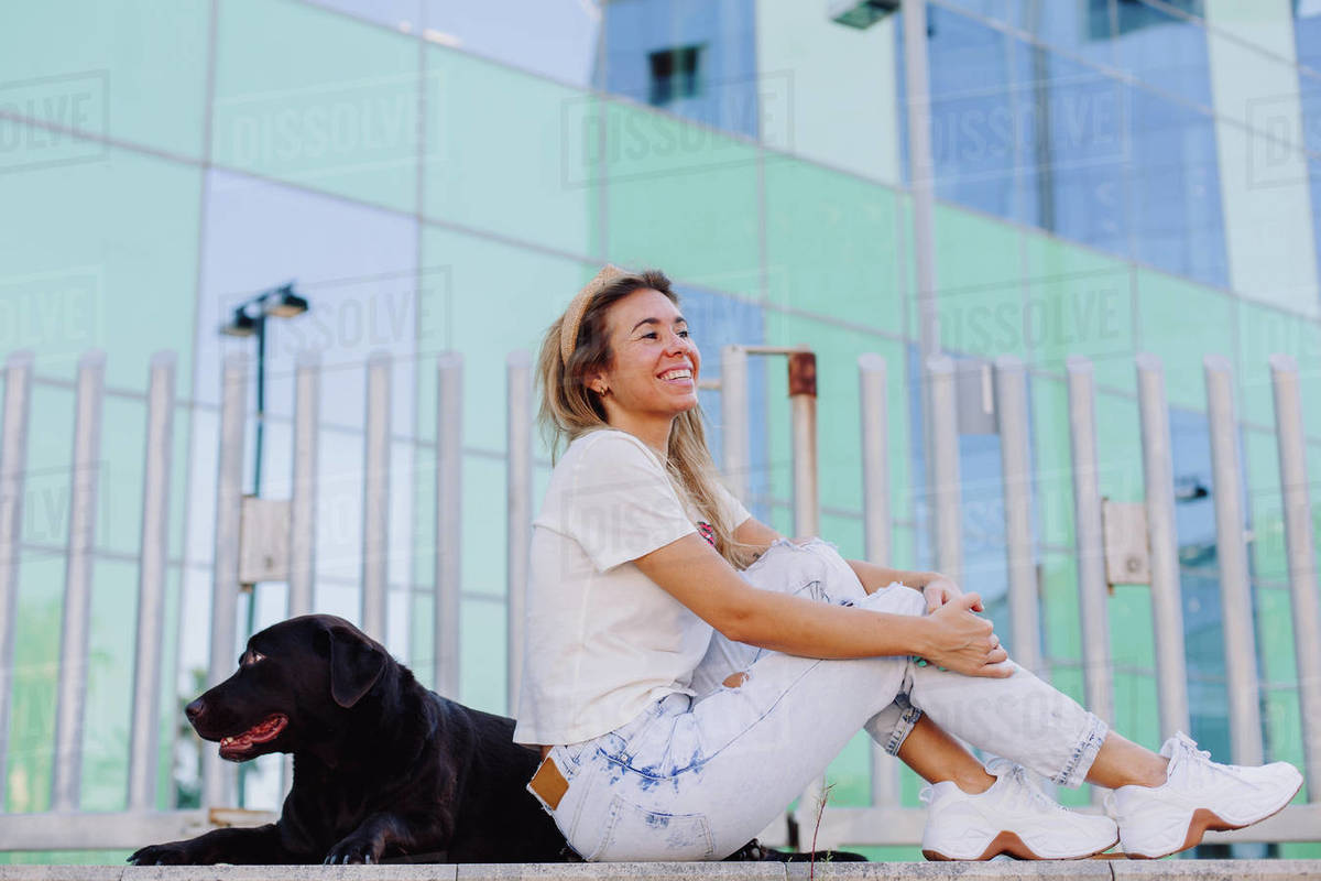 Side view of female in summer wear sitting on bench with obedient ...