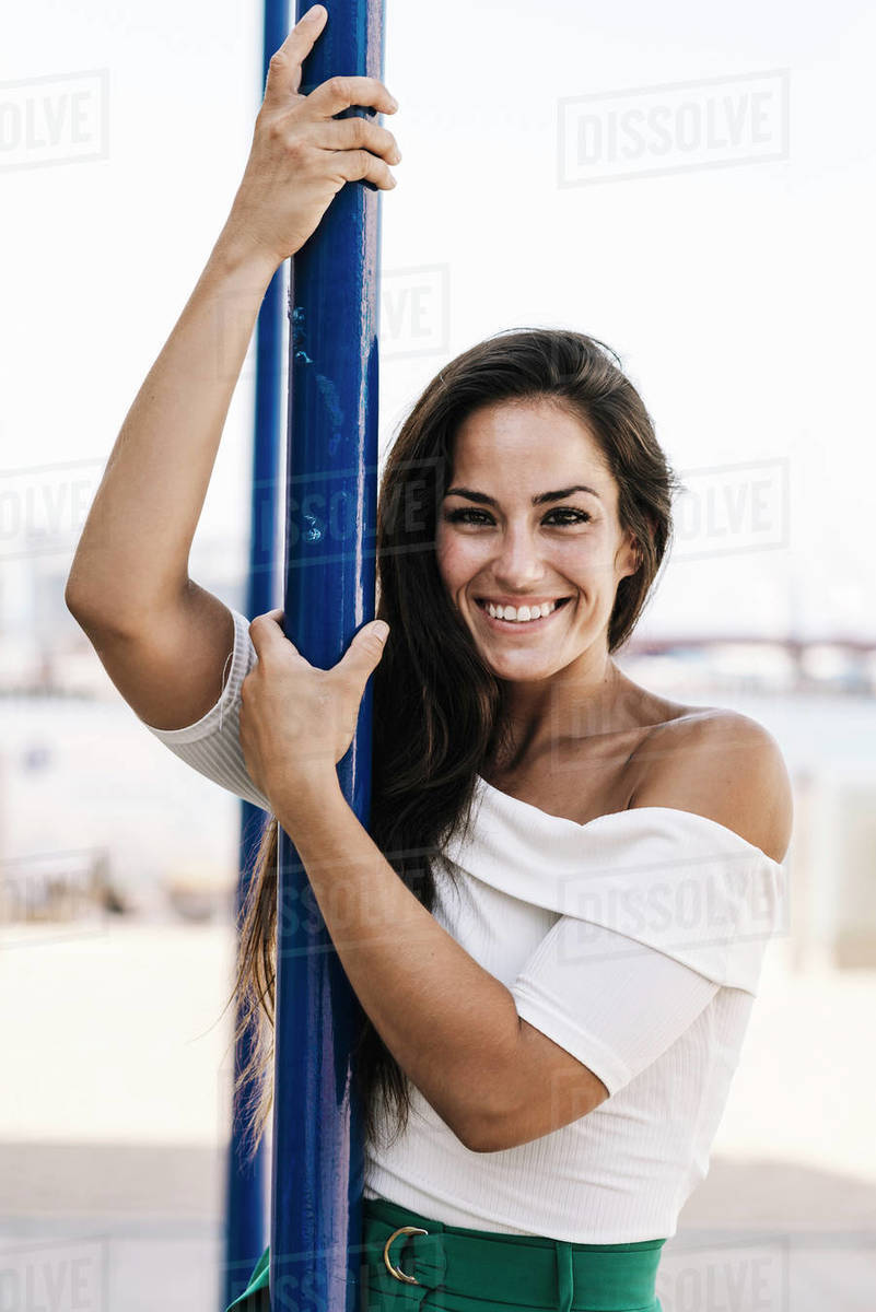 Beautiful smiling young woman hanging on a pole in the street while ...