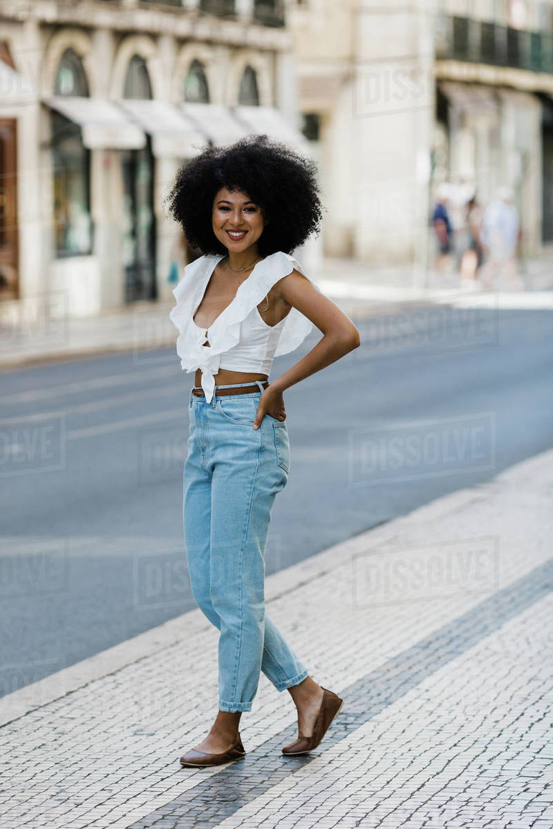 Happy ethnic woman in trendy outfit and looking at camera on summer day ...