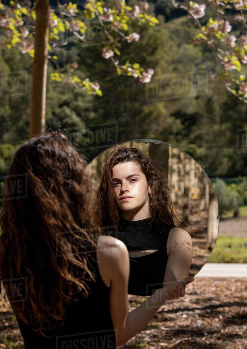 Back view of pretty brunette female in black top reflected in round ...