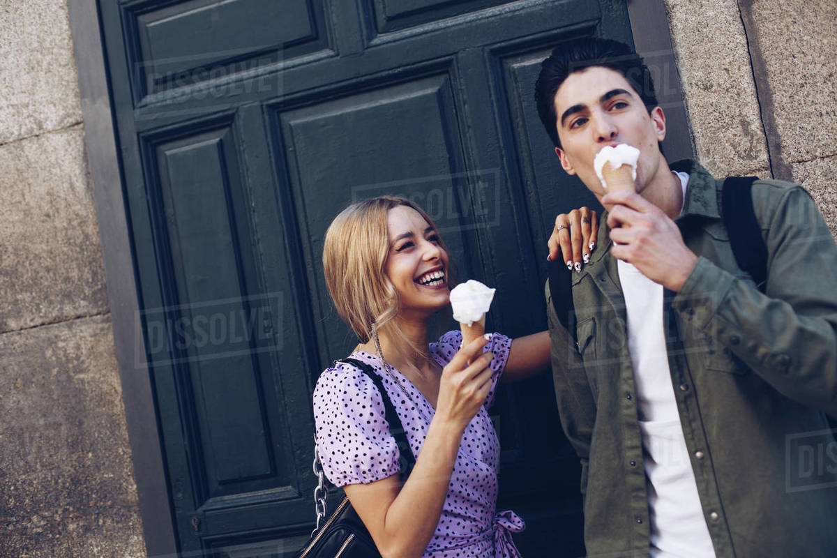 Cheerful young attractive woman and boyfriend eating cornet of ice ...