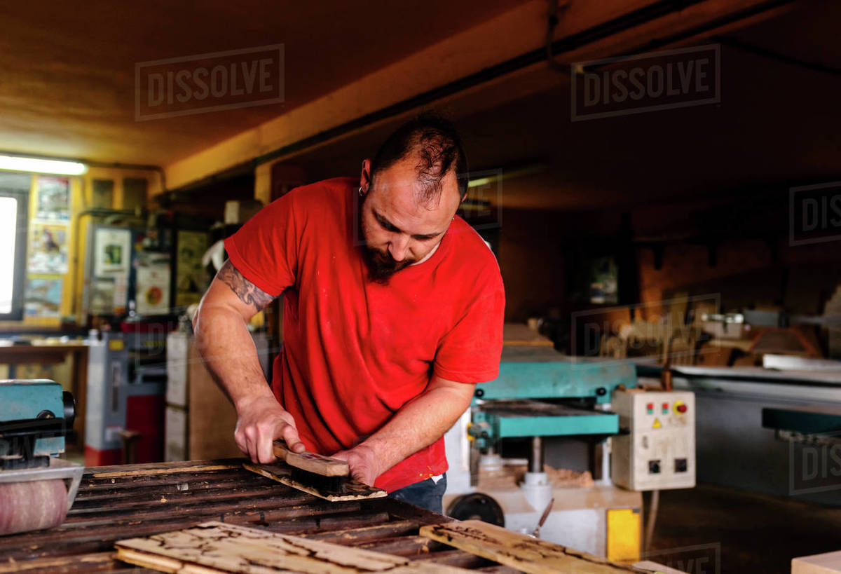 Busy male woodworker standing at workbench and polishing timber plank ...