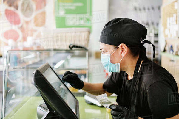 Side view serious female cashier wearing gloves and mask tapping on ...