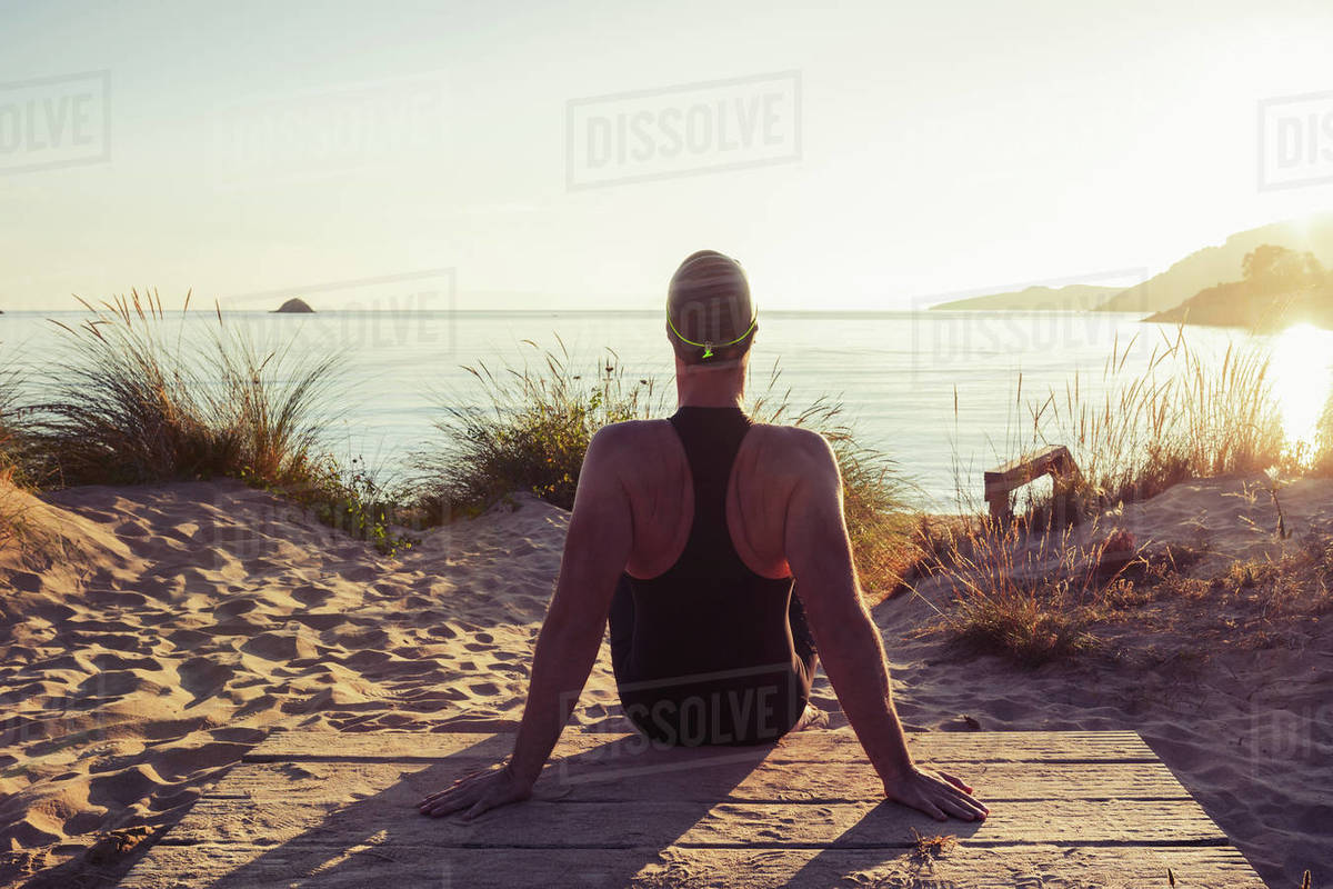 Back view of fit professional swimmer sitting along wooden pathway ...