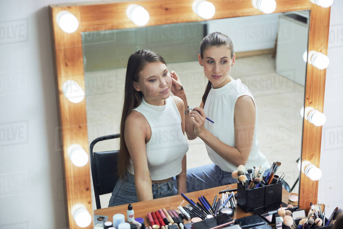 Positive young female makeup artist doing clients face makeup using ...