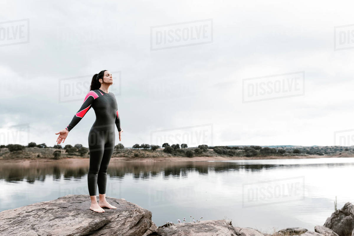 Side view of barefoot female with eyes closed diver in wetsuit standing ...