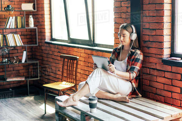 Young barefoot female student in headphones studying while watching ...