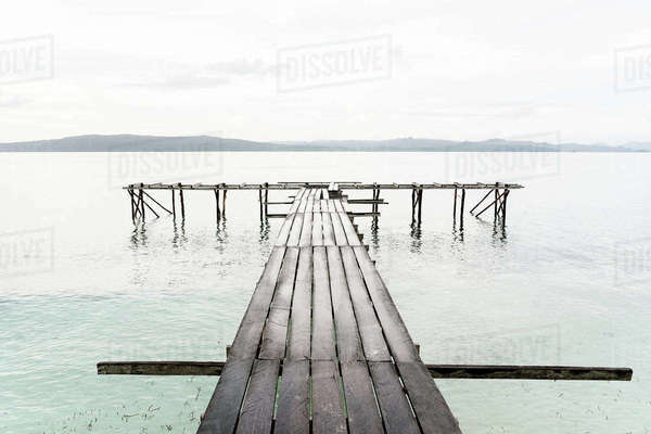 Shabby wooden quay in clean water of pond on background of mountains on ...