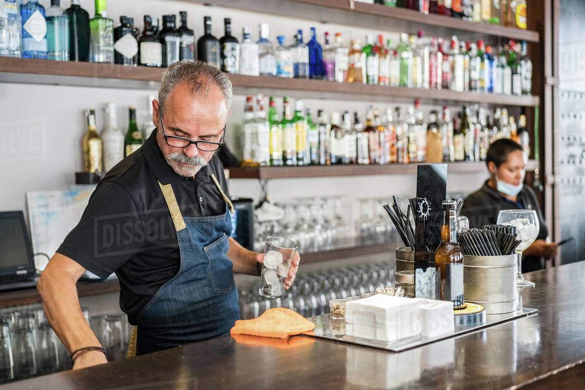 Side view of male and female bar coworkers making drinks during working ...