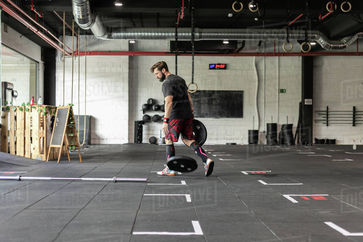 Fit male weightlifter standing in modern gym with barbell and heavy ...