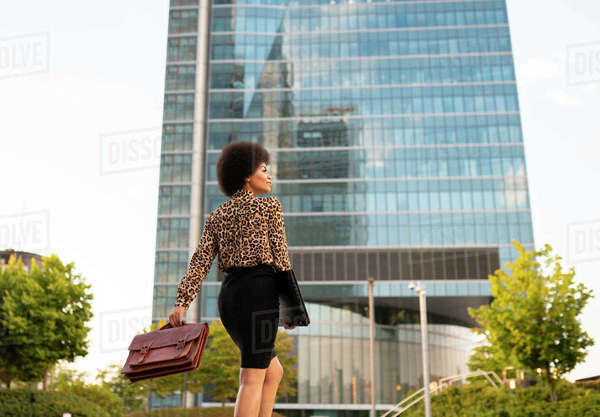 Back view of well dressed African American female worker carrying bag ...