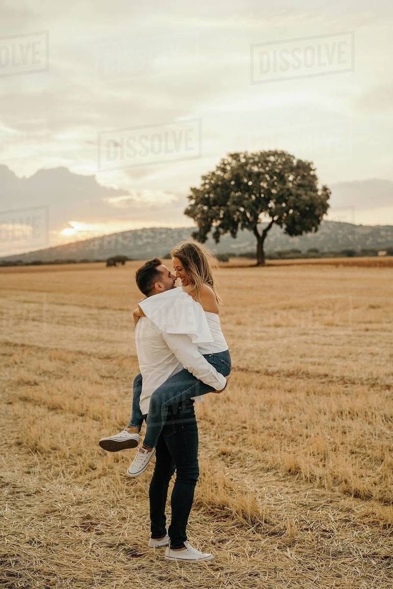 Side view of happy man hugging and carrying girlfriend while standing ...