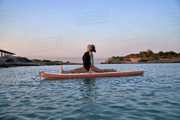 Side view of flexible female in swimsuit performing Front Splits while ...