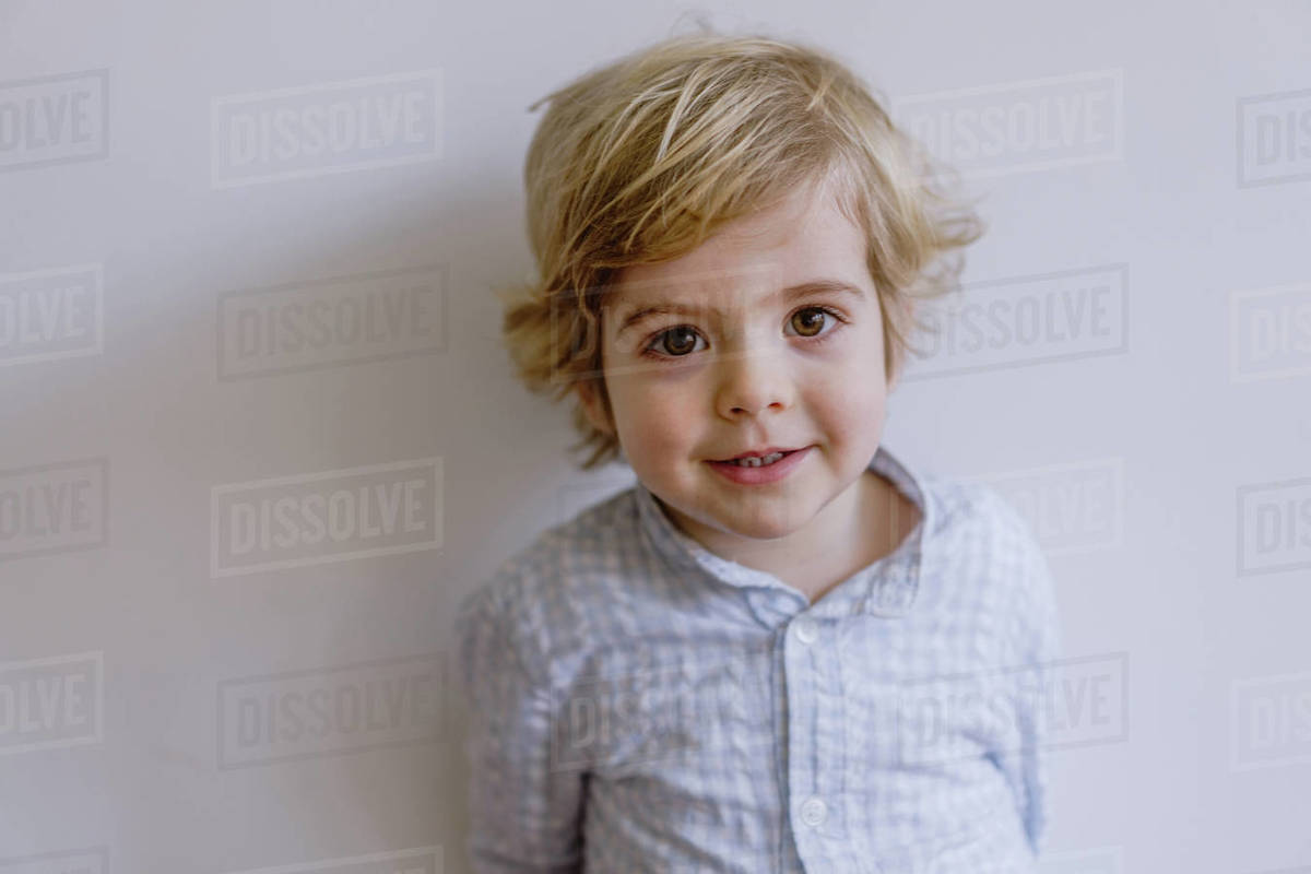 Adorable content child in casual shirt standing near while wall and ...