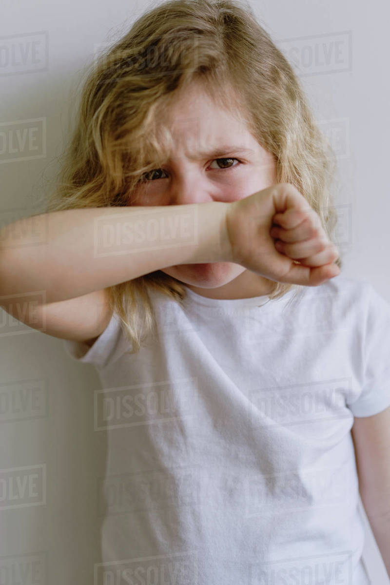 Naughty kid with wavy hair in casual clothing standing with folded arms ...