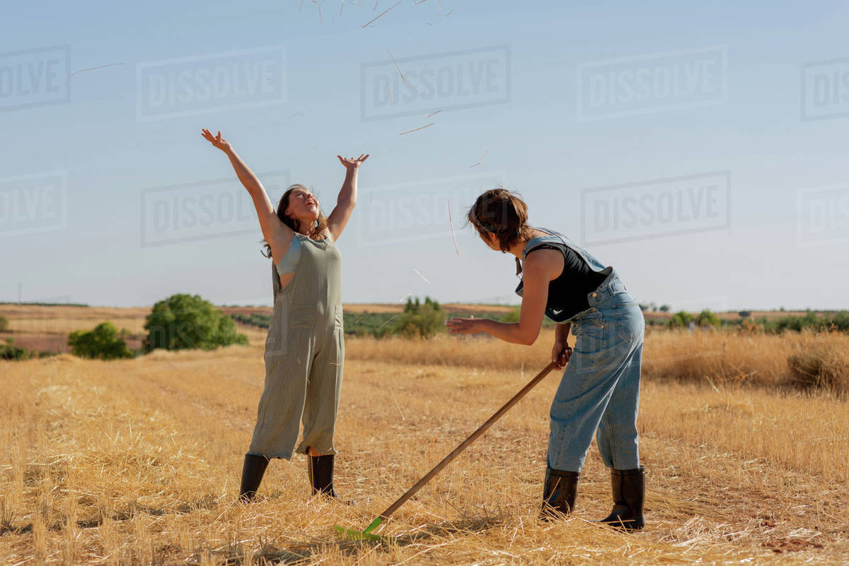 Side view of delighted female friends standing in dry field and ...