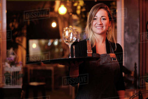 Confident adult hostess smiling and holding tray with two goblets of ...