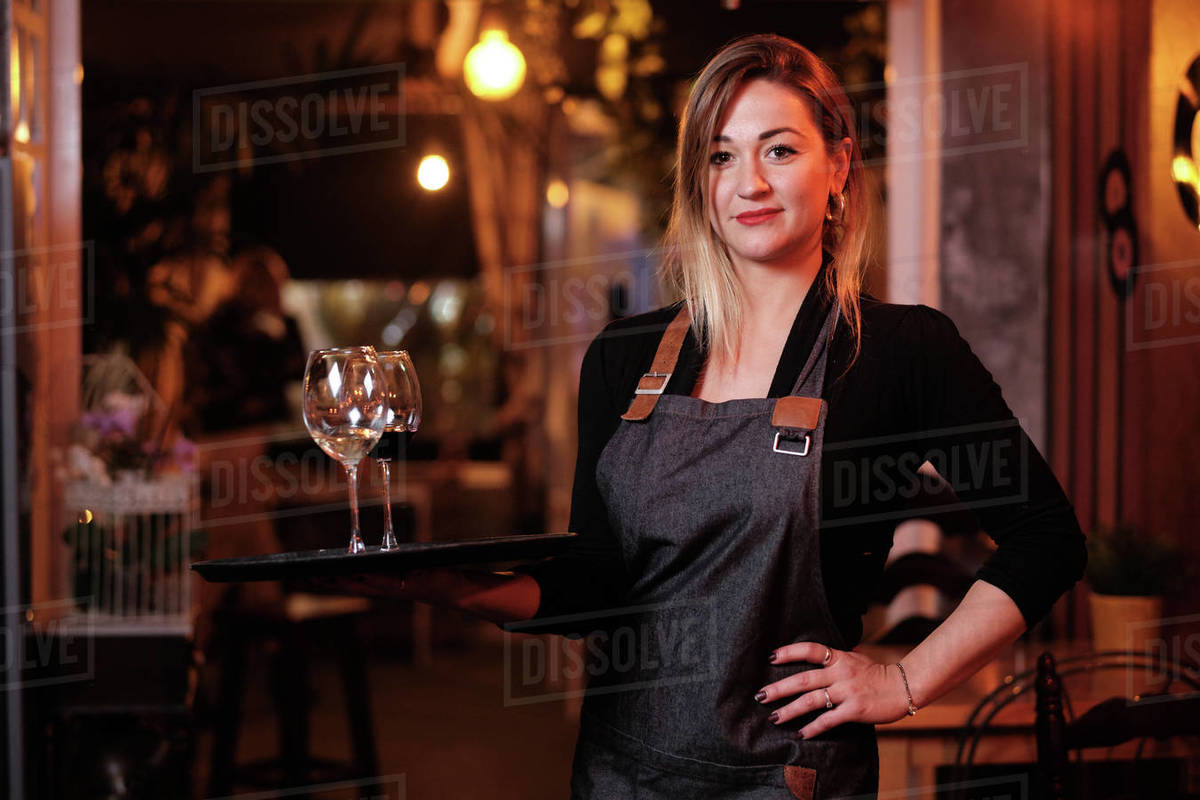 Confident adult hostess smiling and holding tray with two goblets of ...
