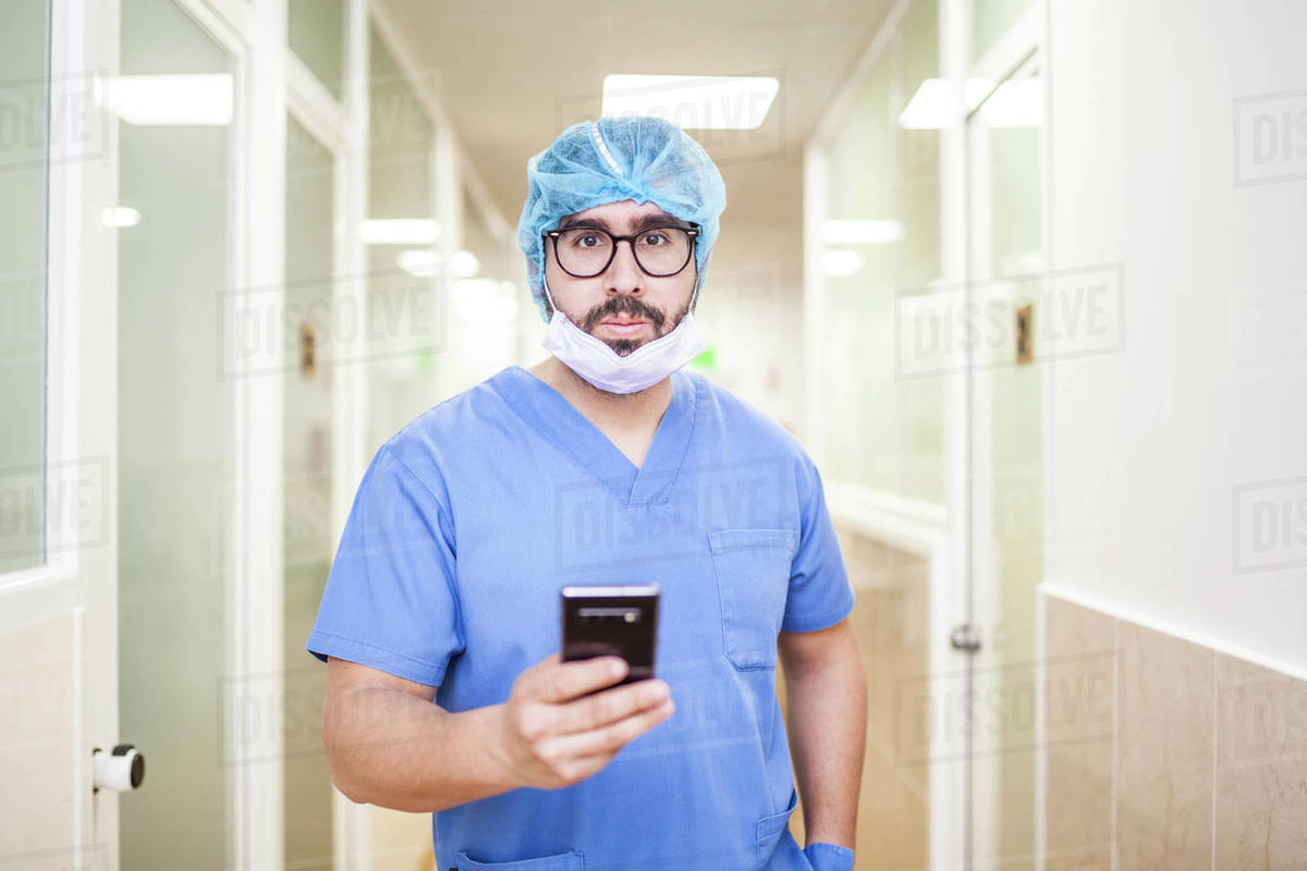 Male surgeon standing in the hallway while checking messages on his ...