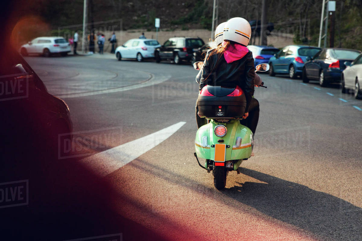 Back view on green scooter with person in helmet driving on asphalt ...