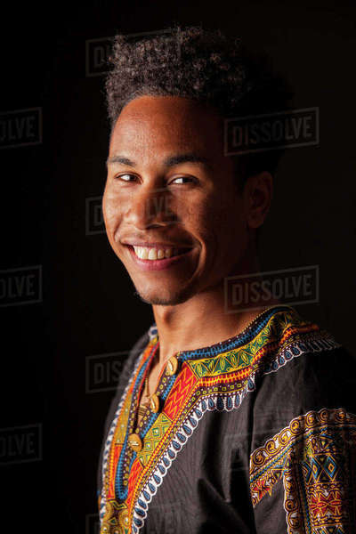 Side view of young African man in ethnic clothing looking at camera and ...