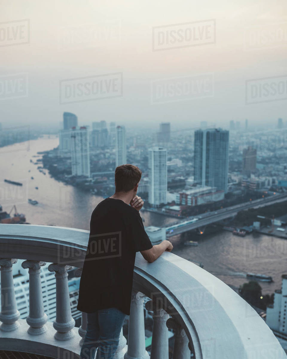 Back view of man standing on skyscraper balcony looking at cityscape in ...