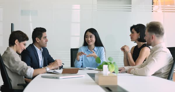 Positive young Asian team leader woman talking to multiethnic ...