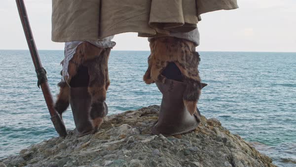 A medieval knight with an ax stands on a stone and looks out to sea ...