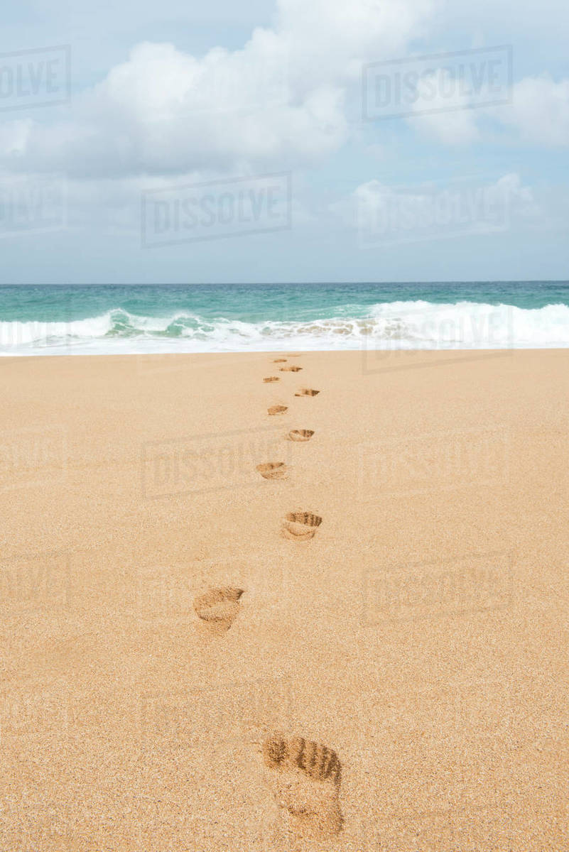 Footsteps on the beach leading into the ocean in the Hawaiian island of ...