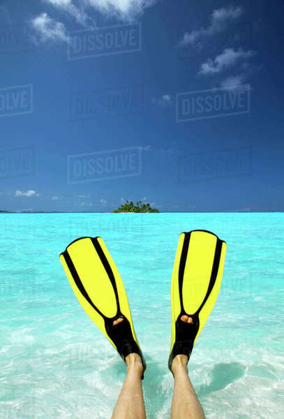 Tropical island and person wearing flippers sitting in sea, Maldives ...