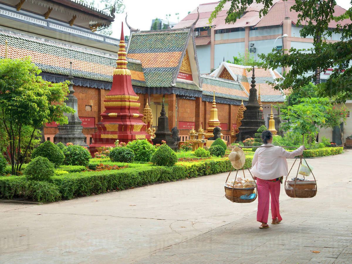 Woman carrying baskets over her shoulders outside a temple in Siem Reap ...