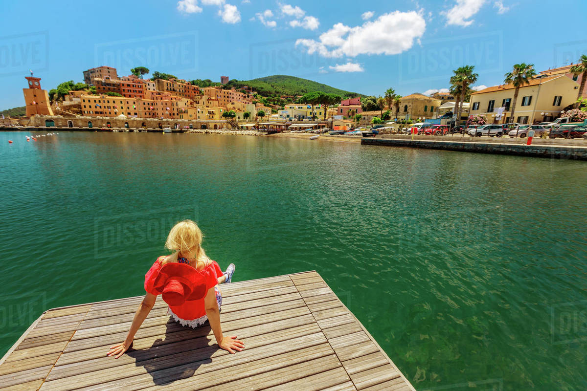 Blonde woman in red suit resting and sunbathing on jetty in Rio Marina ...