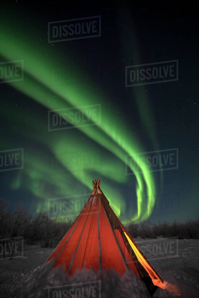 A swirling Aurora Borealis (Northern Lights) over a traditional Sami ...
