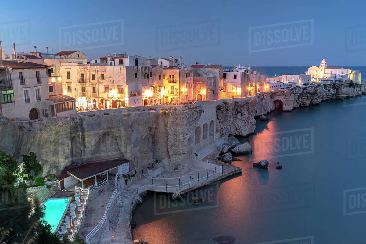 Illuminated pool of luxury resort by the sea at dusk in Vieste old town ...