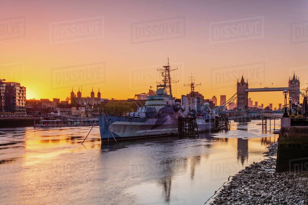 HMS Belfast and Tower Bridge at sunrise with a low tide on the River Thames, London, England ...