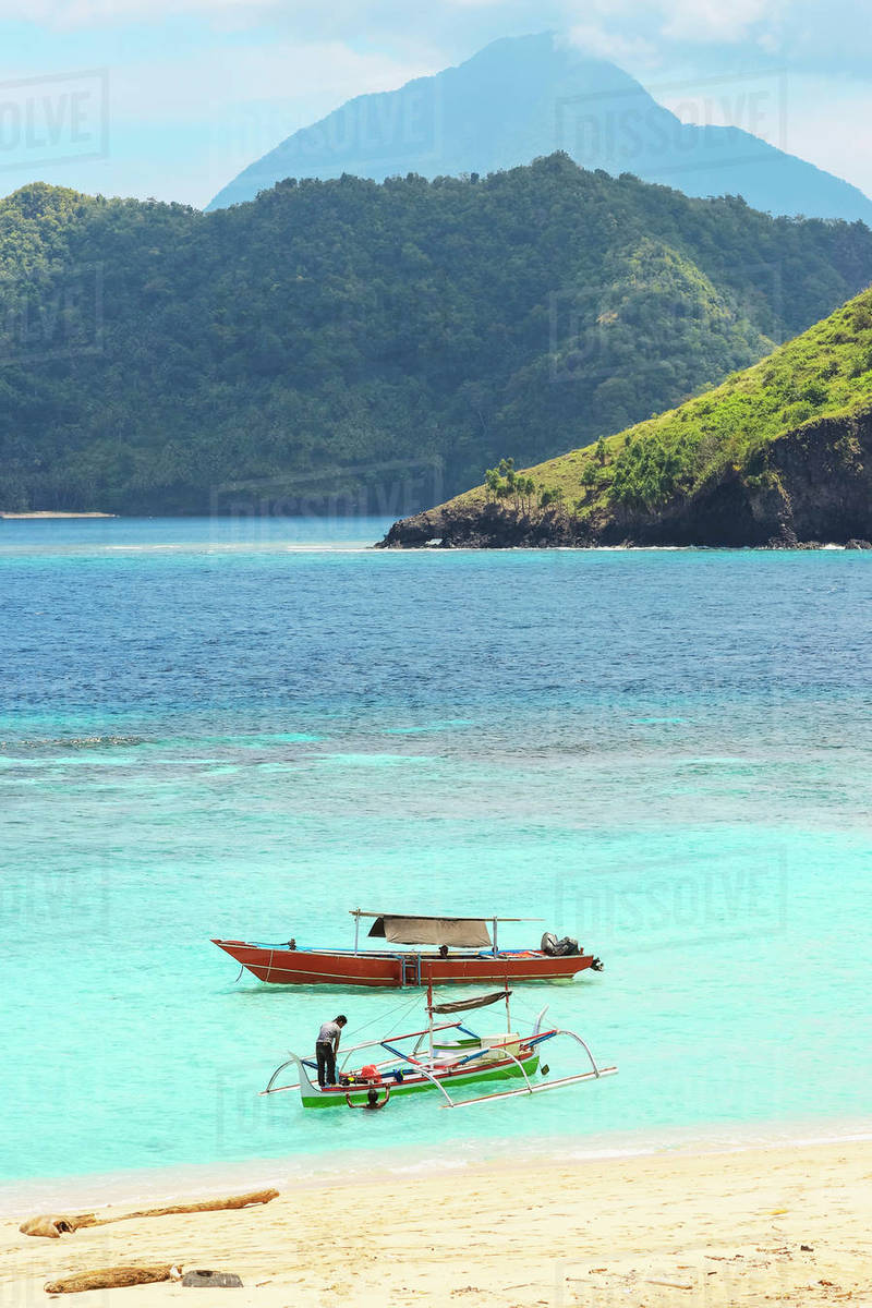 Mahoro Island beach with tour boats and a volcano far beyond on Siau ...