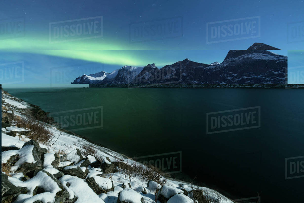 Northern Lights and stars over Senjahopen peak surrounded by the frozen ...