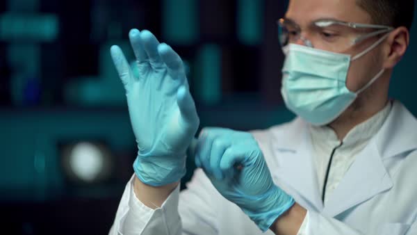 A lab worker in a mask puts on protective work glasses for working in ...