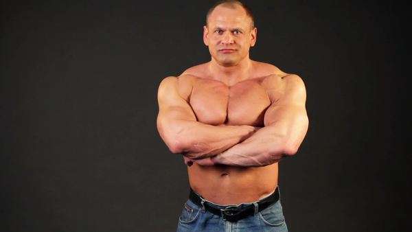 Bodybuilder in jeans shows his muscular body lit at dark background ...